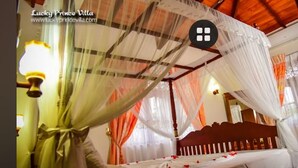 Quarto com cama de dossel, cabeceira de madeira e janela com cortinas.