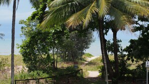 Um parque com um banco de madeira, um caminho que leva à praia e uma placa indicando uma trilha para caminhada.