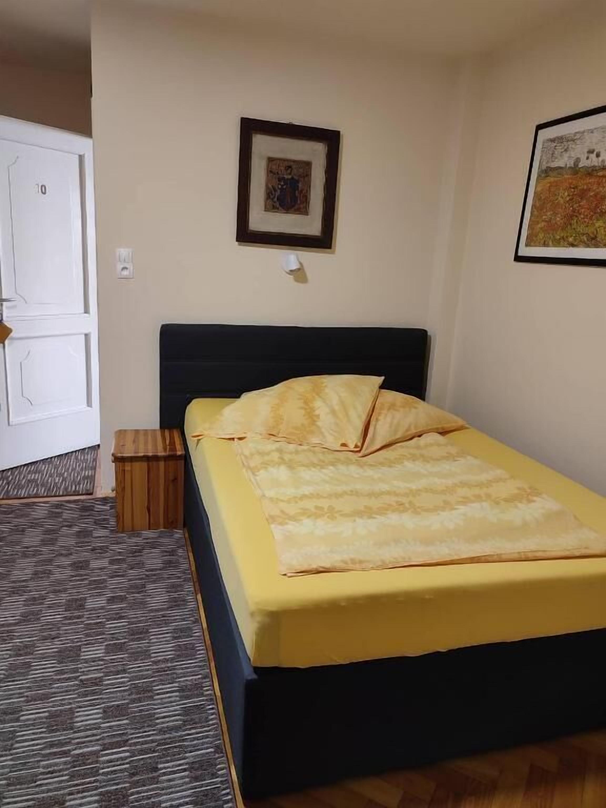 Quarto com cama, mesa de cabeceira, porta e um quadro na parede.
