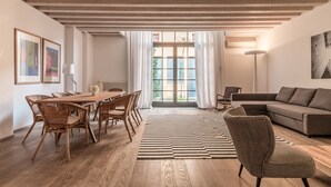 Uma sala de estar moderna com uma mesa de jantar de madeira, cadeiras de vime, tapete listrado, sofá cinza e uma grande janela com cortinas.