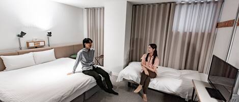 Quarto de hotel com duas camas, uma mesa com computador e uma TV na parede.