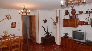 Sala de estar com área de jantar, móveis de madeira, televisão e lustre.