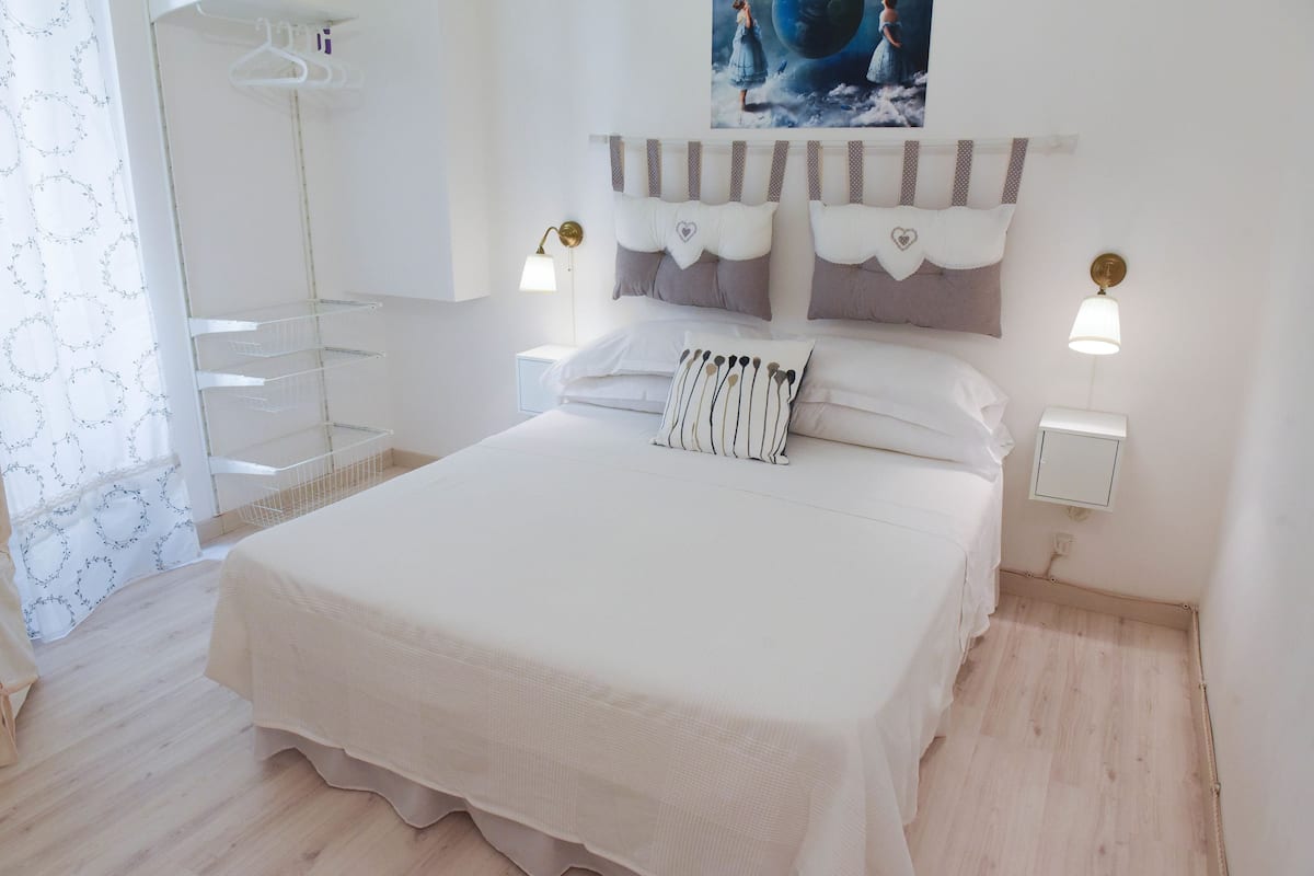 Quarto bem organizado com cama, mesas de cabeceira e prateleira na parede.