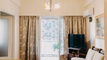 Uma sala de estar com televisão, sofá, lustre e varanda com cortinas.