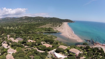 Uma área costeira com praia, casas e montanhas ao fundo.