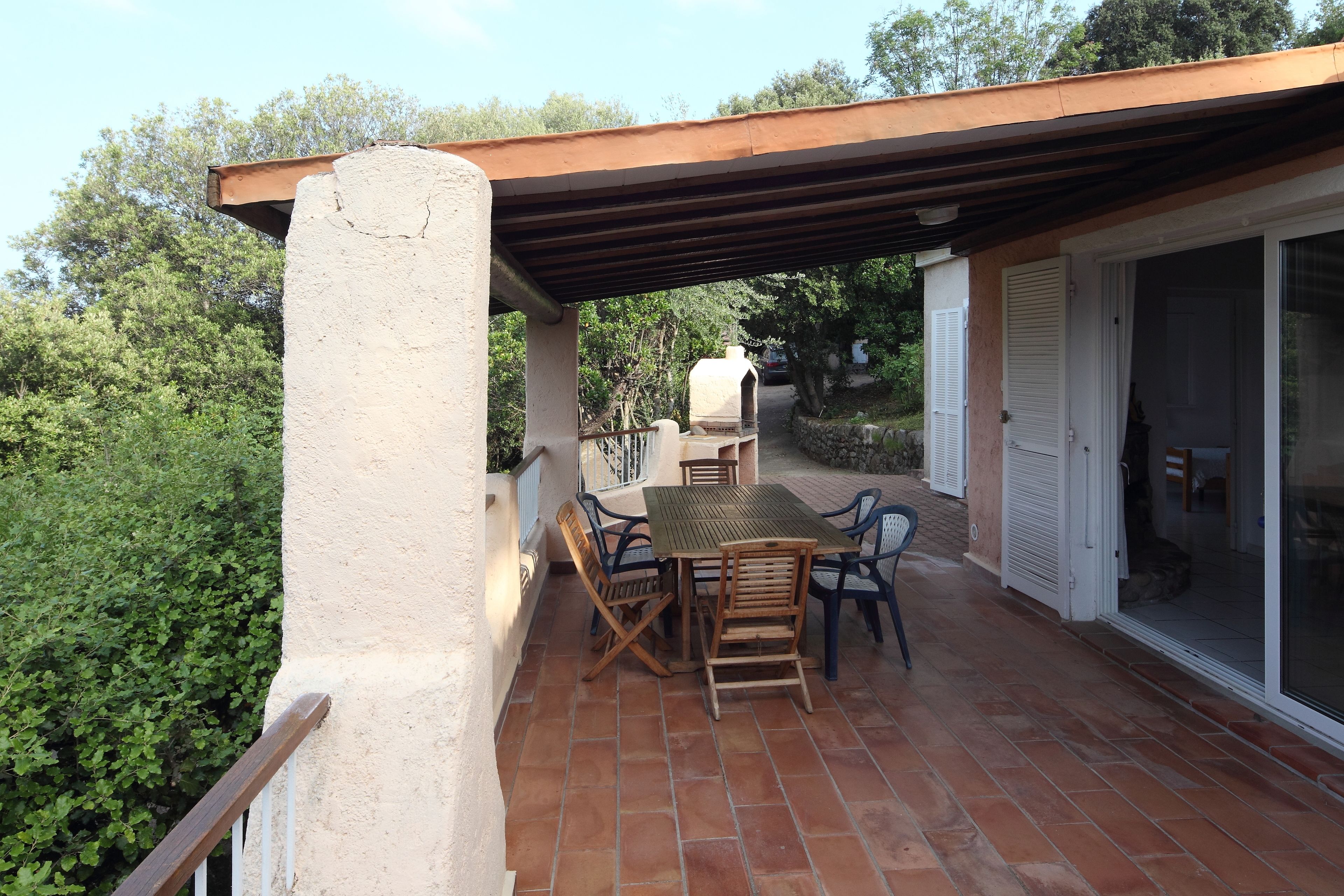 Um pátio externo com mesa e cadeiras, churrasqueira e área coberta com pérgola.