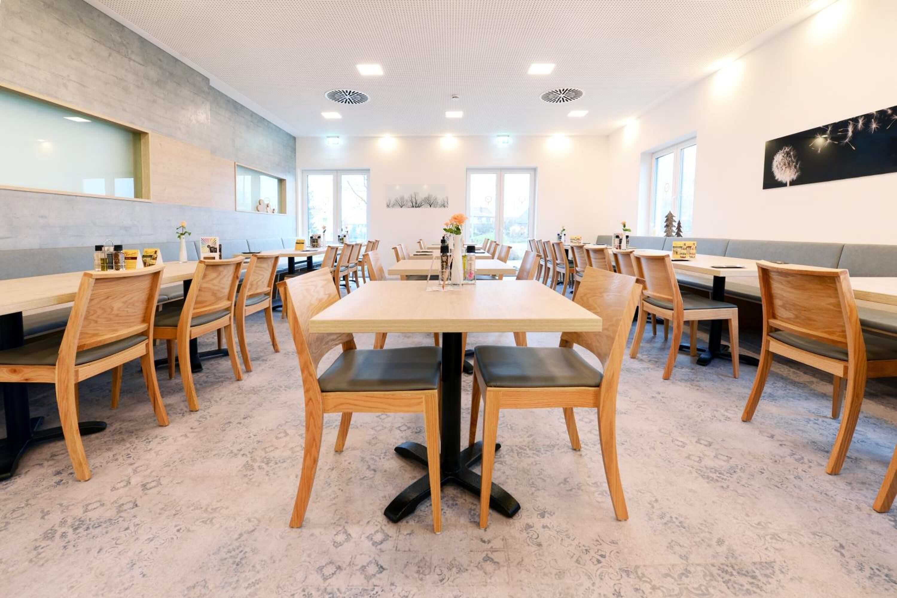 Uma sala de jantar espaçosa com várias mesas e cadeiras de madeira, janelas amplas e um design de teto moderno.