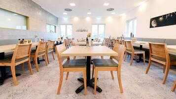 Uma sala de jantar espaçosa com várias mesas e cadeiras de madeira, janelas amplas e um design de teto moderno.