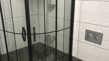 Divisória de chuveiro com porta de vidro, vaso sanitário e bidê.