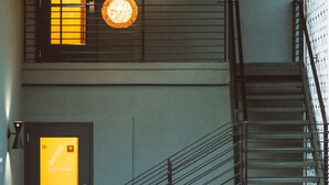 Interior de hotel com vários níveis, uma escadaria, portas de acesso para hóspedes e luminárias pendentes.