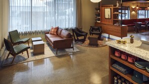 Um hall de hotel moderno com um sofá de couro, cadeiras verdes, um balcão de recepção de madeira e uma área de bar.