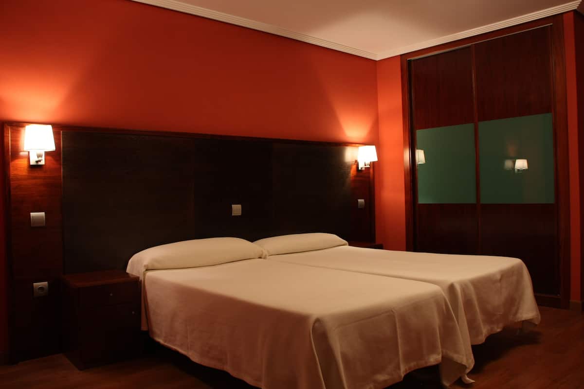 Uma cama de casal com cabeceira de madeira e duas luminárias laterais.
