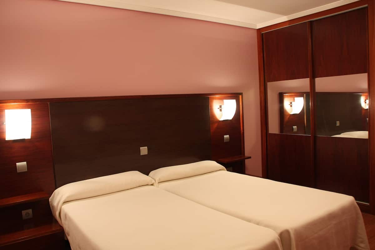 Quarto de hotel com cama de casal, cabeceira de madeira, espelho e mesa de cabeceira.