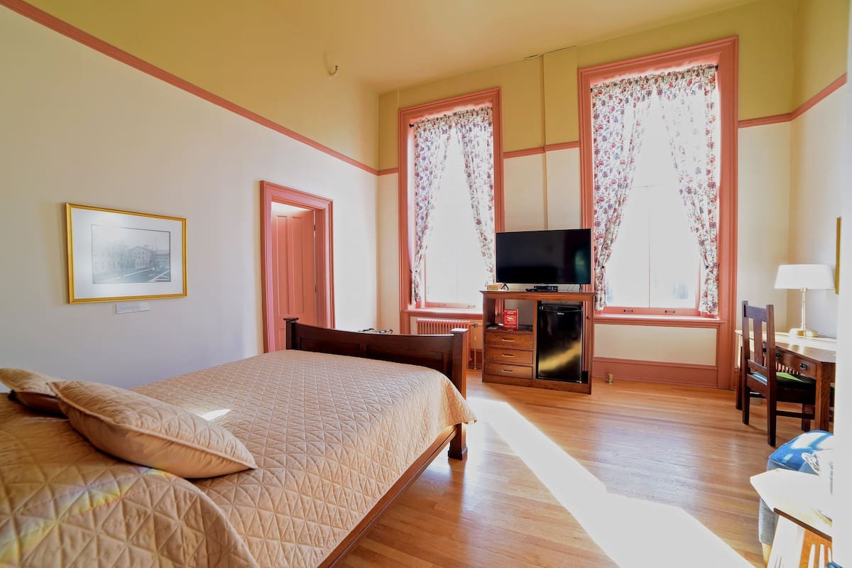 Quarto de hotel com cama, televisão, escrivaninha e cadeira.