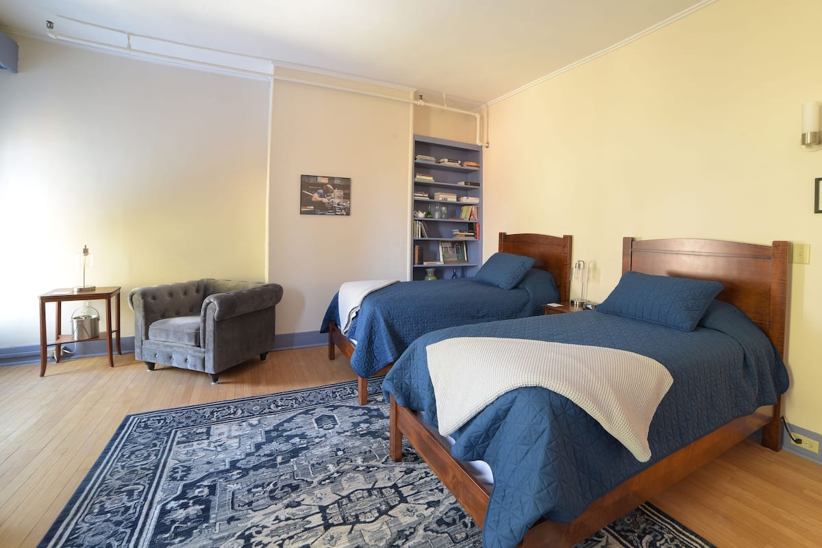 Quarto com duas camas, uma estante, uma cadeira e um tapete.