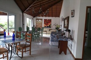 Uma ampla área de refeições com mesas e cadeiras de madeira, balcão de cozinha e uma grande janela que oferece luz natural.