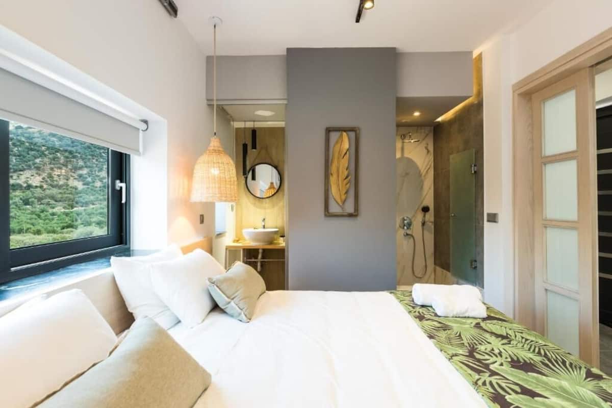 Quarto de hotel moderno com uma cama grande, banheiro com chuveiro e vista para o exterior.