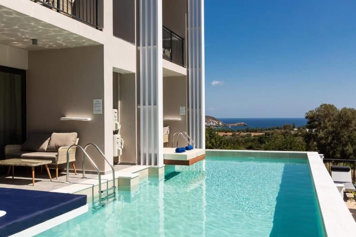 Piscina moderna de hotel com água azul cristalina, uma espreguiçadeira e vista para o mar.