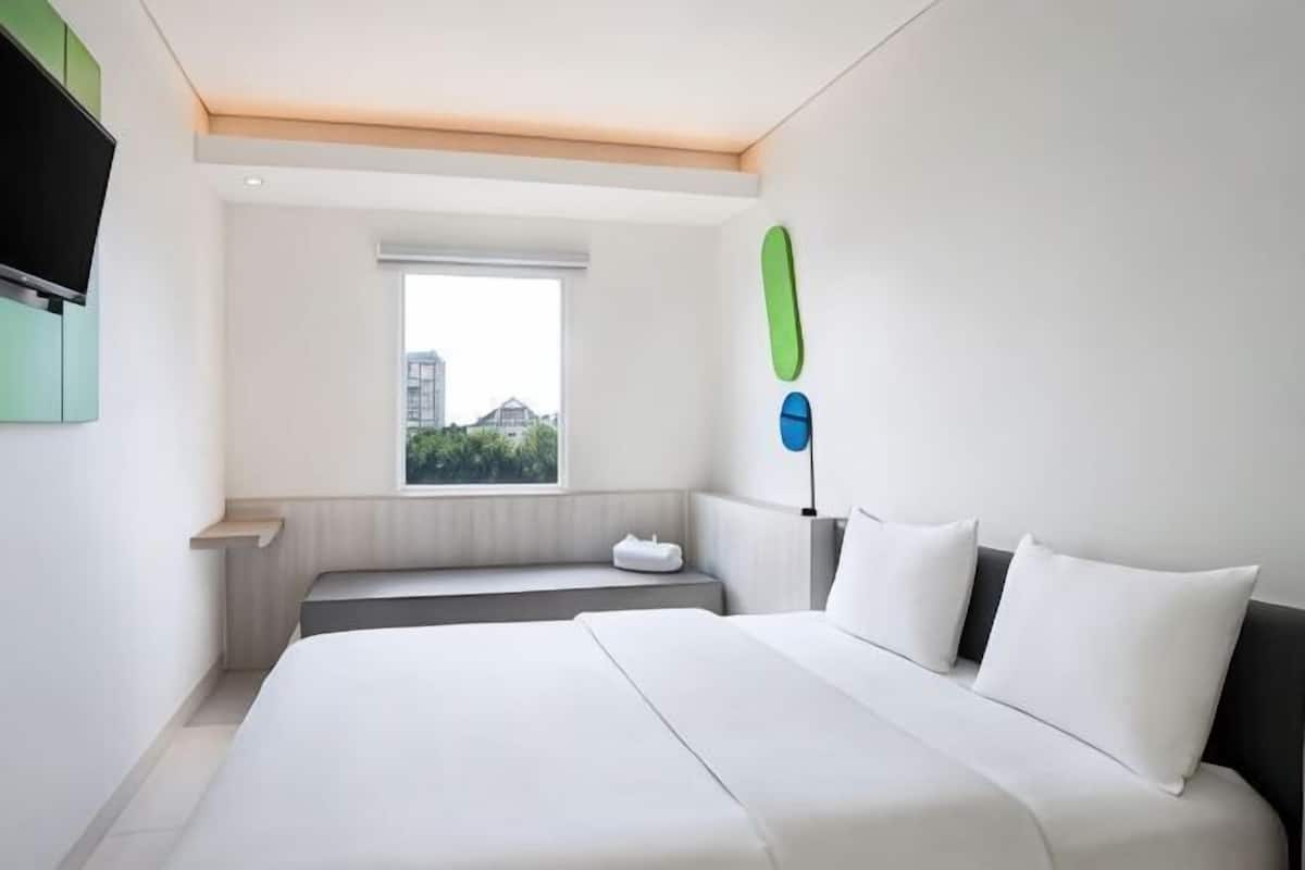 Quarto de hotel moderno com uma cama grande, janela com vista para a cidade, televisão de tela plana e um pequeno espaço de estar.