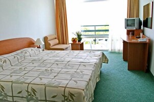 Quarto de hotel com uma cama grande, uma cadeira, uma mesa de trabalho com televisão e uma varanda com vista.