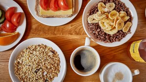 Mesa de café da manhã com cereais, torradas, café e um prato de sobremesa.