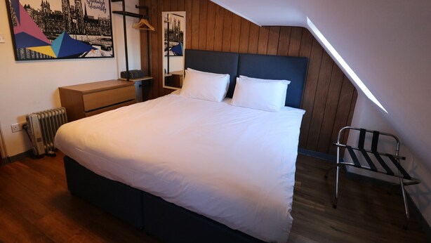 Quarto com cama grande, paredes de painel de madeira, um radiador, uma cadeira e um quadro na parede.