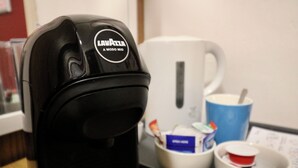 Máquina de café com etiqueta, uma chávena branca e uma chávena azul sobre um tabuleiro.