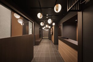 Corredor moderno de hotel com uma receção de madeira, chão em azulejo e lanternas de papel suspensas.
