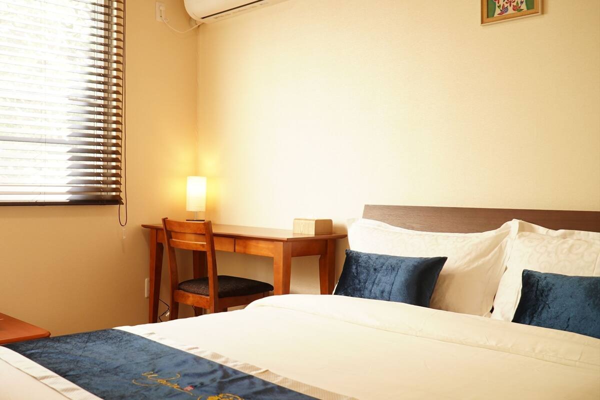 Quarto de hotel com cama, escrivaninha, cadeira e janela com persianas.