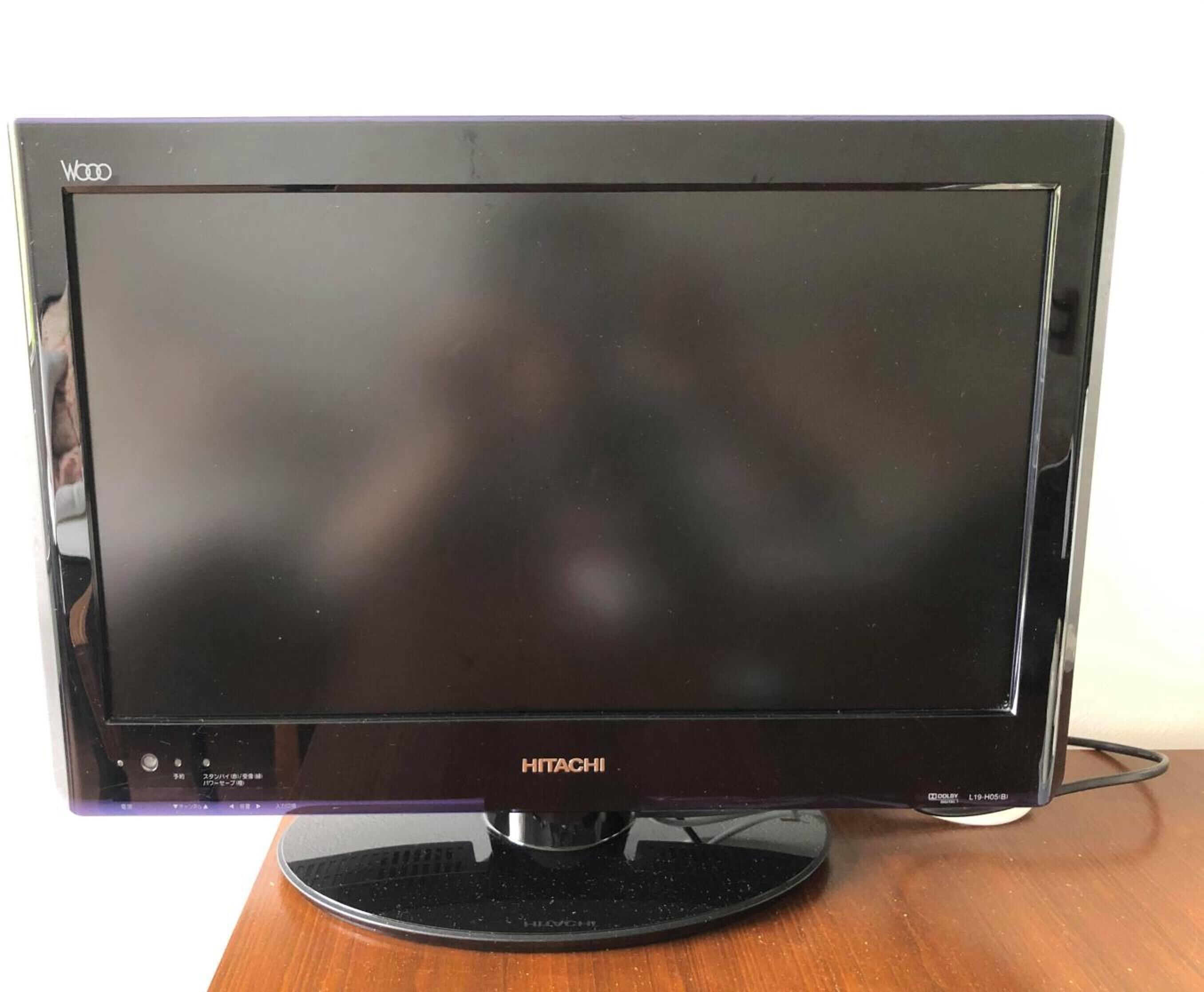 Um monitor Hitachi com tela preta, apoiado em uma superfície de madeira.