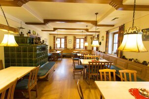 Restaurante com mesas e bancos de madeira, luminárias pendentes e parede revestida com azulejos verdes.