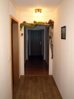 Um corredor com soalho de madeira, uma porta escura no final e um candeeiro em cima.