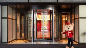 Entrada de hotel com porta giratória, um mascote de urso e decoração interna vermelha.