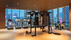 Academia moderna com esteiras, elípticos e equipamentos de musculação, com amplas janelas e vista para a cidade.