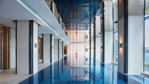 Piscina interior moderna com teto de vidro transparente e uma pessoa na extremidade distante.