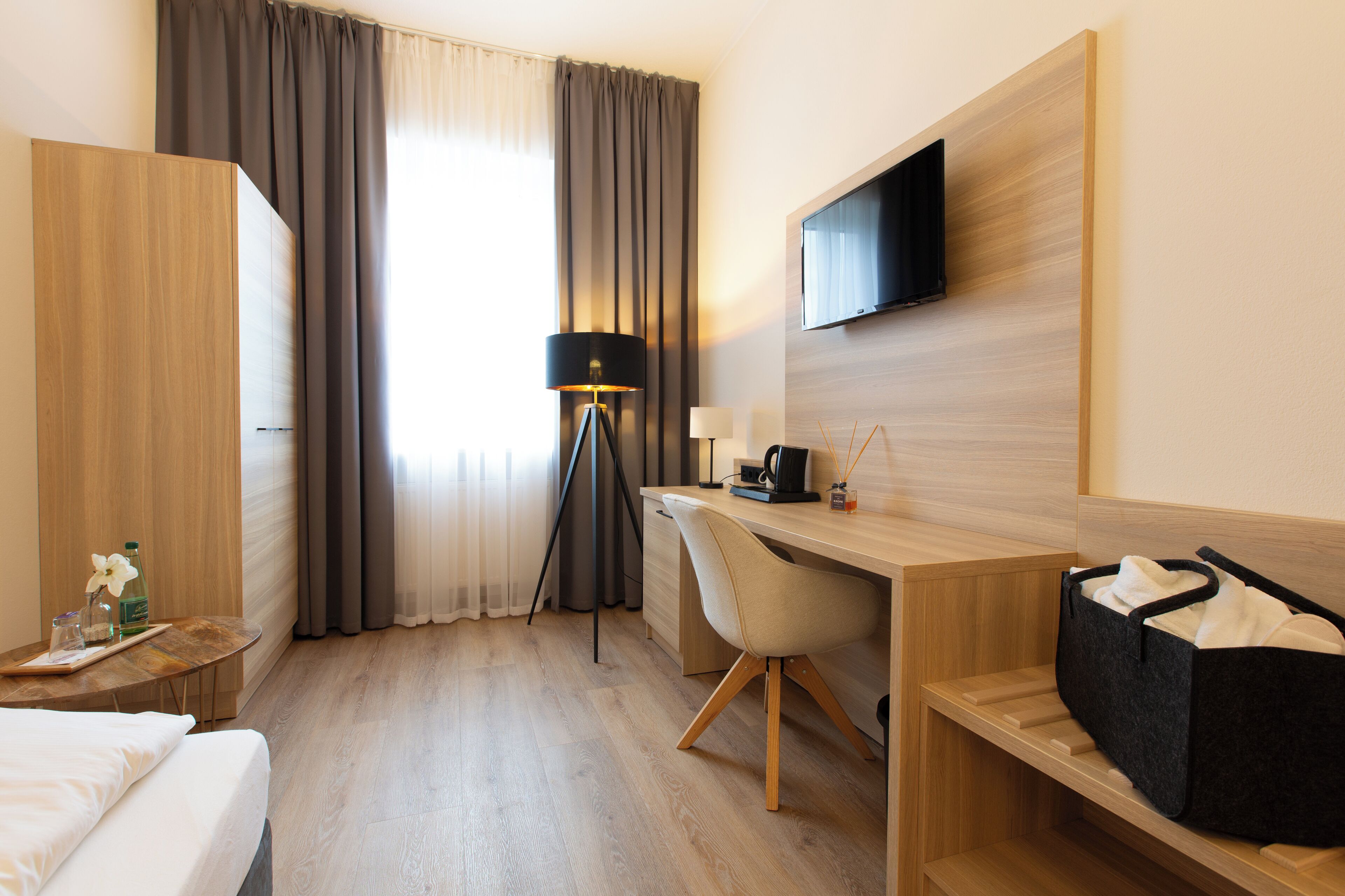 Quarto de hotel com cama, escrivaninha, cadeira e televisão na parede.