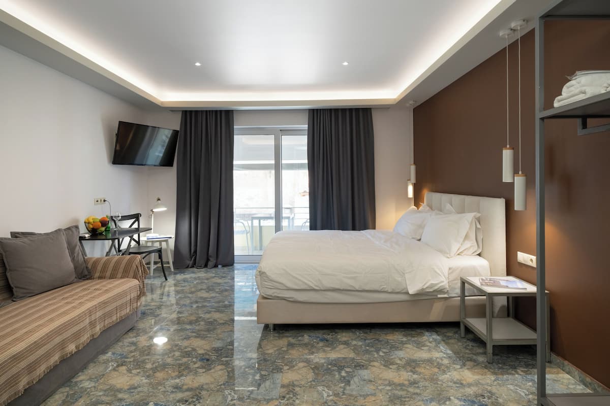 Quarto de hotel moderno com uma cama grande, um sofá, uma escrivaninha e uma televisão.