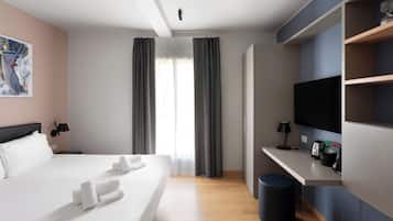 Quarto de hotel com cama, escrivaninha, televisão e janela com cortinas.