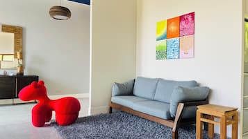 Uma sala de estar moderna com um sofá cinzento, uma pequena mesa de madeira e um quadro abstrato vibrante na parede.