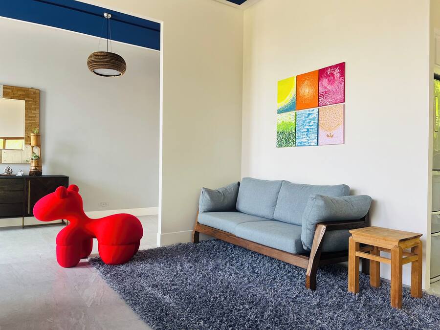 Uma sala de estar moderna com um sofá cinzento, uma pequena mesa de madeira e um quadro abstrato vibrante na parede.