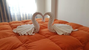 Uma cama com um edredom laranja e duas toalhas em formato de cisne.