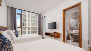 Quarto de hotel com duas camas, televisão, banheiro com pia e uma janela grande com cortinas.