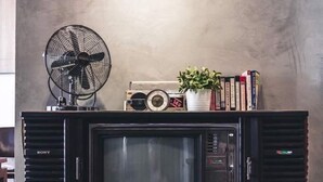 Um televisor Sony antigo montado em um suporte de madeira, com um pequeno ventilador e um vaso de planta em cima.