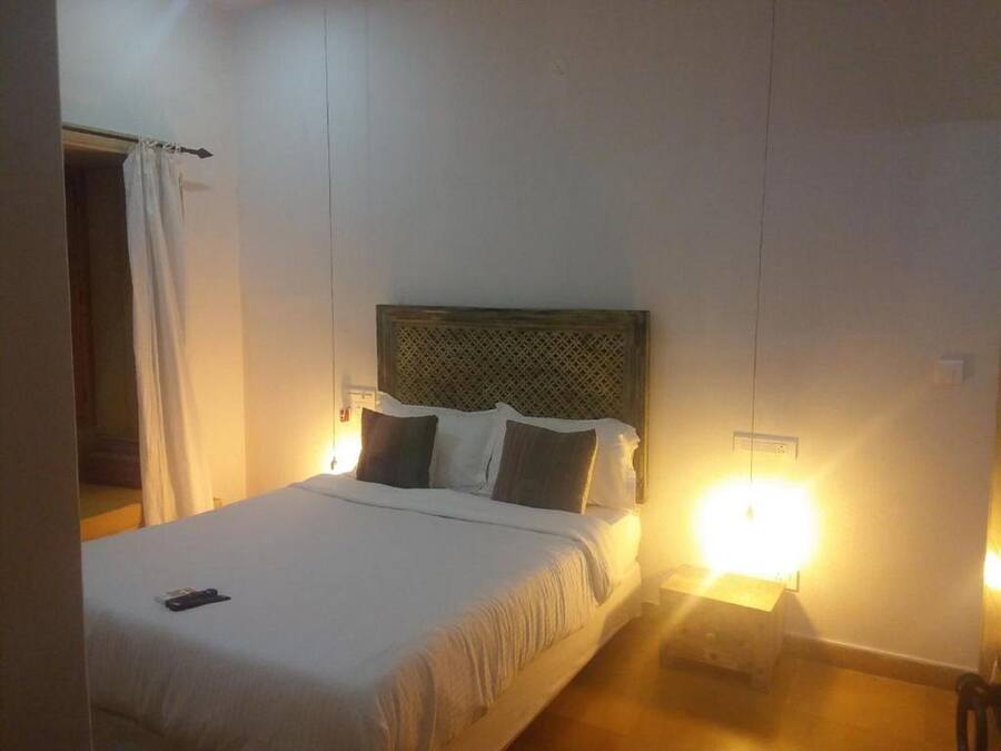 Quarto com cama, duas luminárias de cabeceira, painel de cama em madeira e cortina branca.