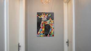 Um corredor com um lustre geométrico e um quadro de uma girafa colorida na parede.