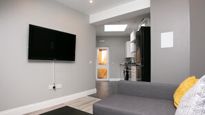 Uma sala de estar moderna com uma TV de tela plana na parede, um sofá cinza e uma mesa de centro preta.