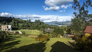 Paisagem rural com uma casa, um pequeno lago e vista para montanhas distantes.