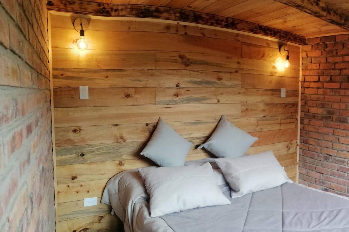 Quarto de cabana de madeira com cama, almofadas e parede de tijolos.