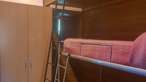 Uma cama beliche com escada, um guarda-roupa e piso revestido de azulejos.