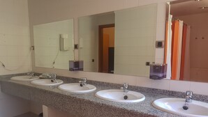 Casa de banho com quatro lavatórios, um espelho grande e zona de duche.